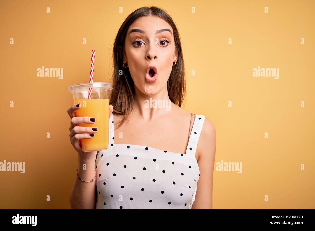 Young beautiful brunette woman drinking healthy orange juice over ...