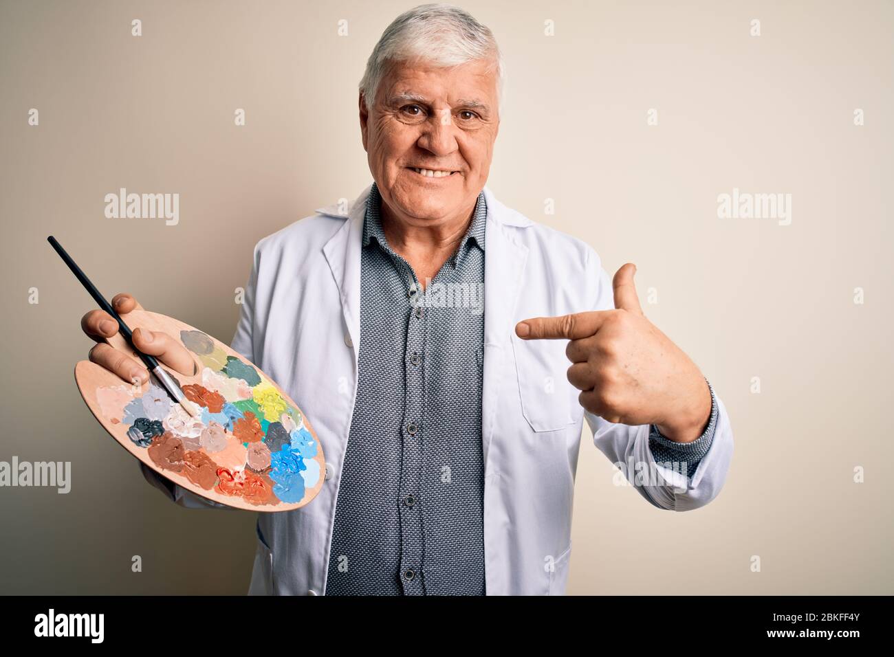 Senior handsome hoary painter man painting using brush and palette with ...