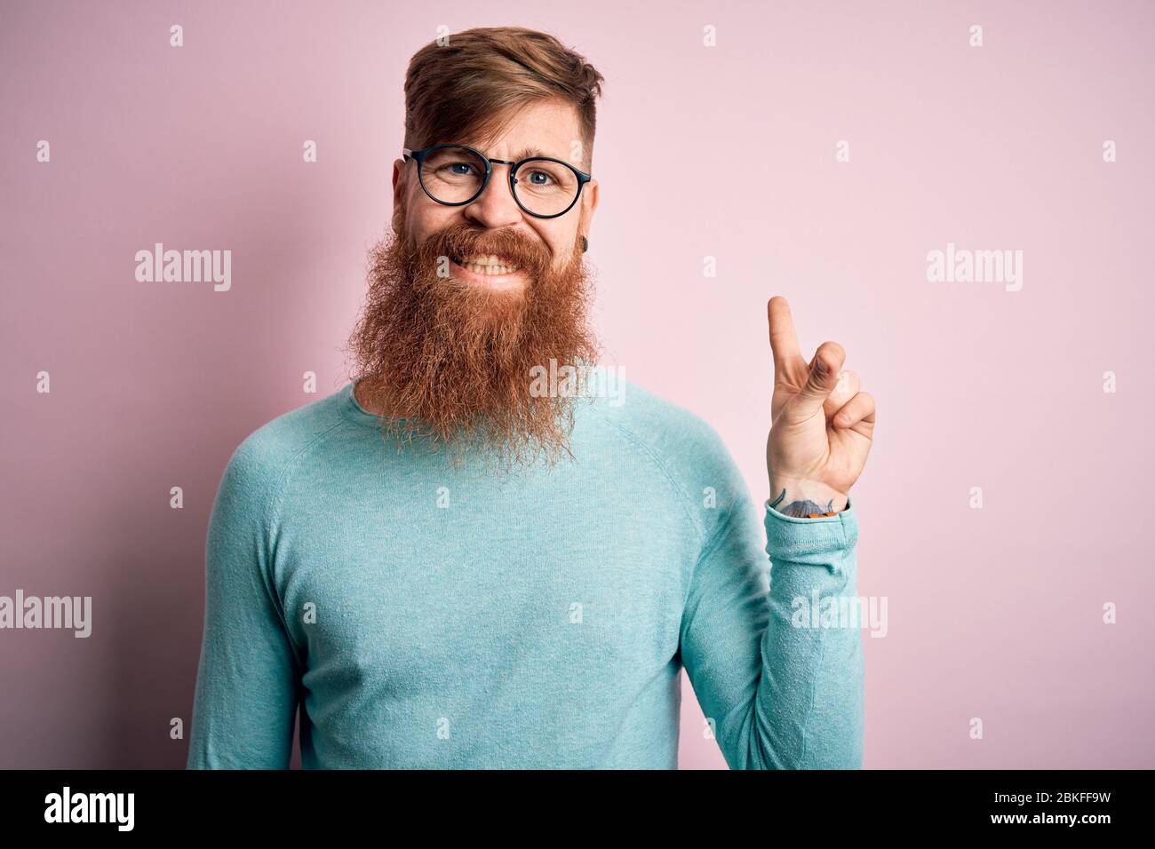 Handsome Irish redhead man with beard wearing glasses over pink ...
