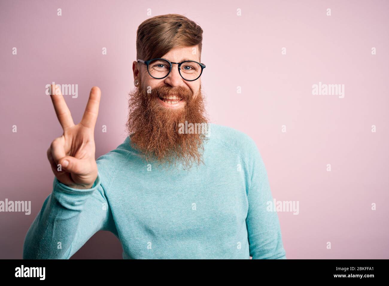 Handsome Irish redhead man with beard wearing glasses over pink ...