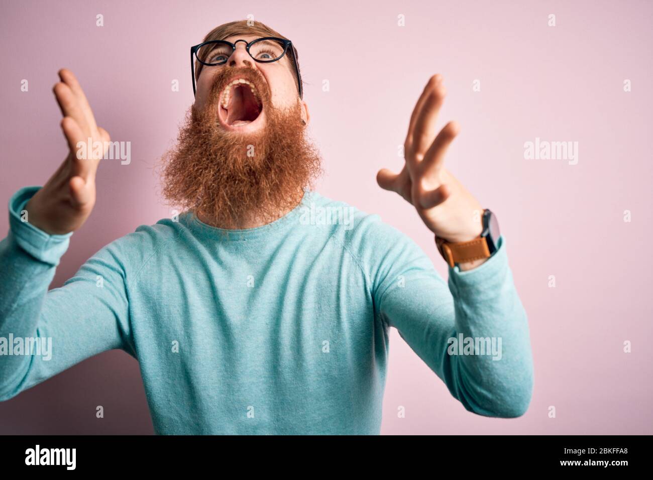 Handsome Irish redhead man with beard wearing glasses over pink ...