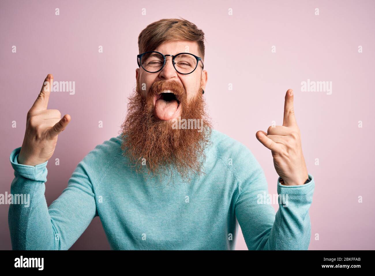 Handsome Irish redhead man with beard wearing glasses over pink ...