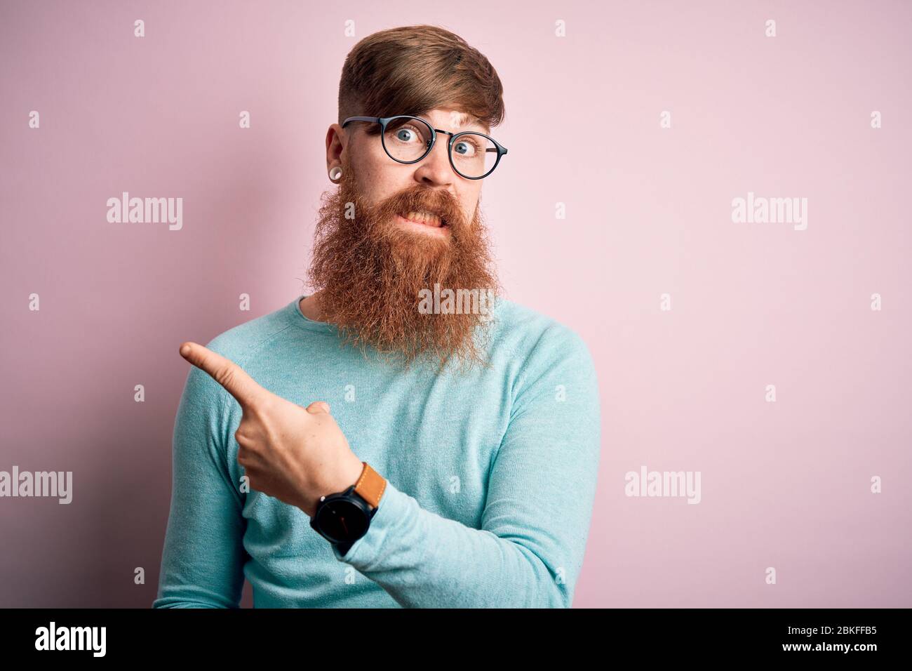 Handsome Irish redhead man with beard wearing glasses over pink ...