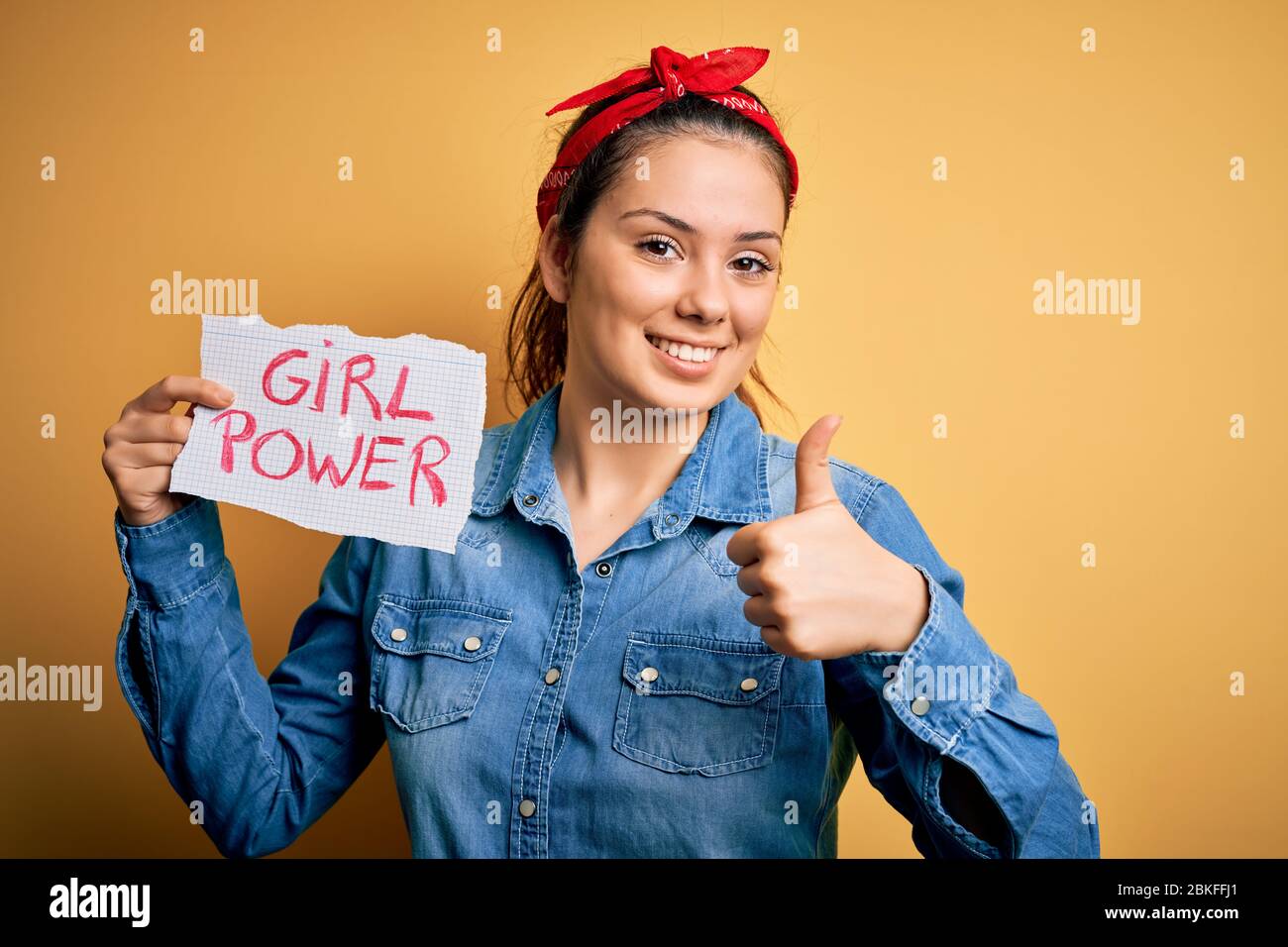 Young beautiful woman holding paper with girl power message over yellow ...