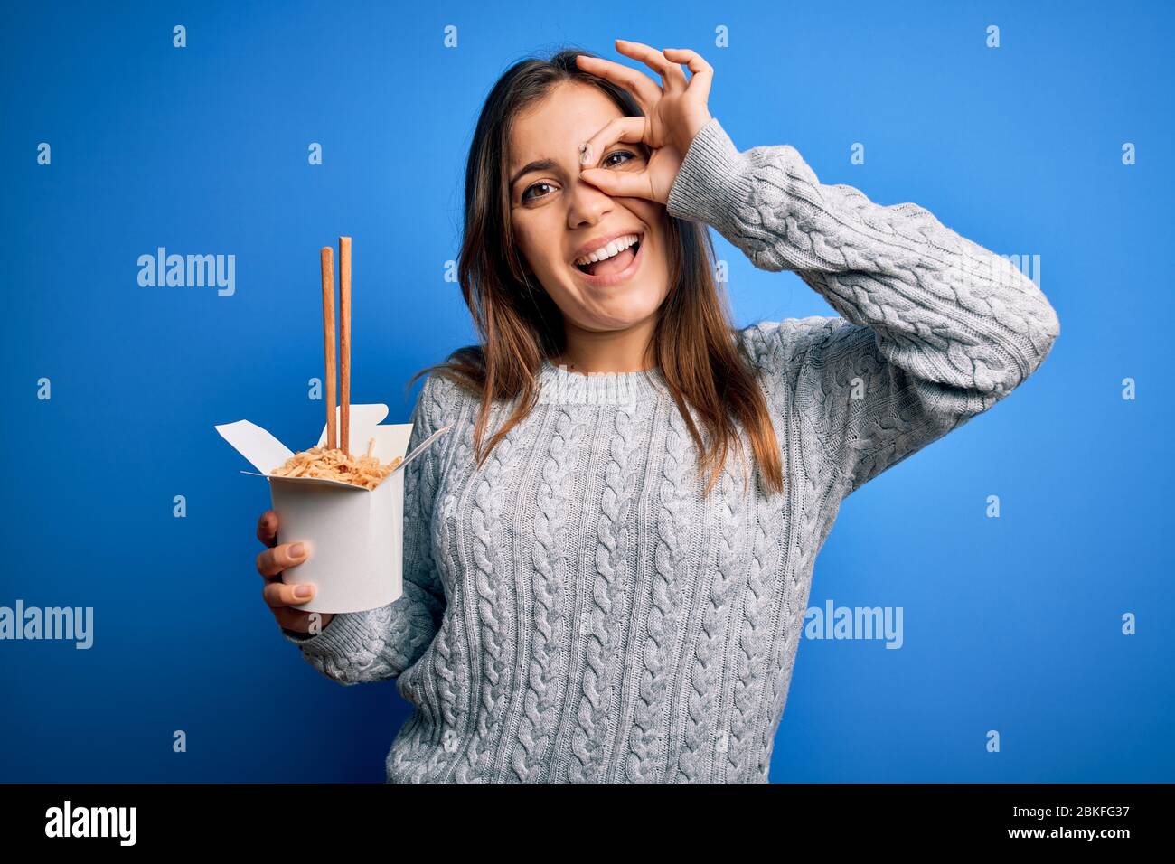 Young woman eating asian noodles from take away box using chopstick ...