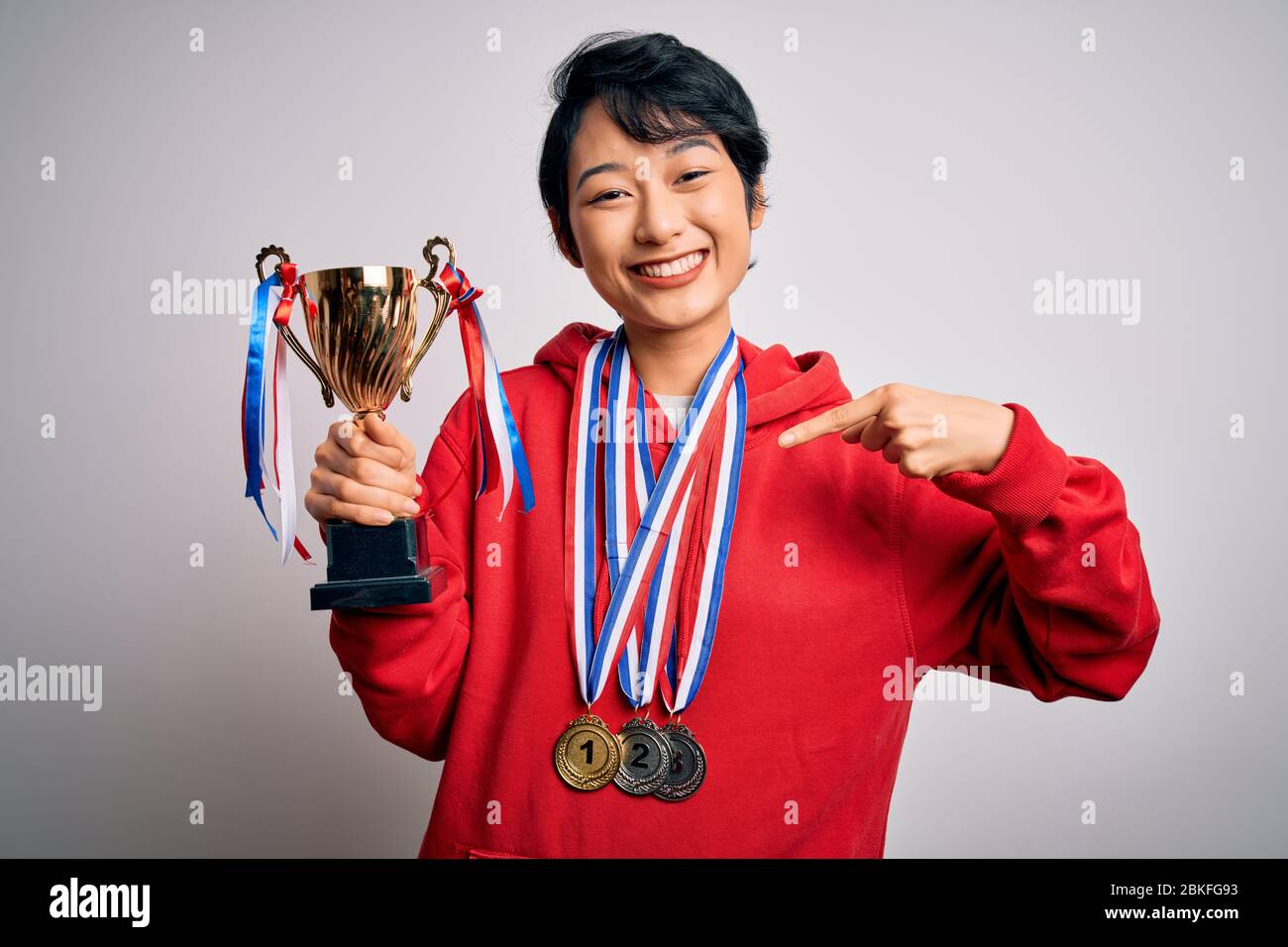 Young beautiful asian girl winner holding trophy wearing medals over ...