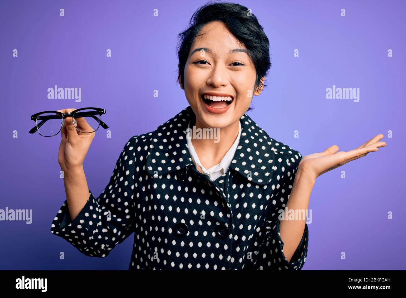 Young beautiful asian optical girl holding vision glasses over isolated ...