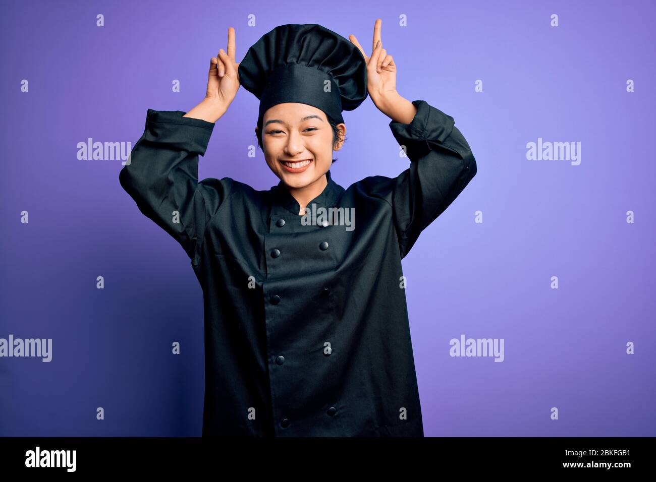 Young beautiful chinese chef woman wearing cooker uniform and hat over ...