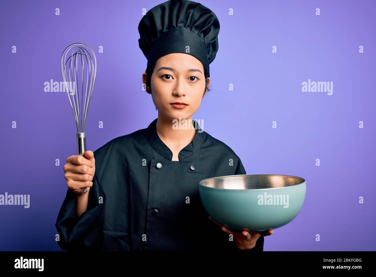 Young beautiful chinese chef woman wearing cooker uniform and hat using ...