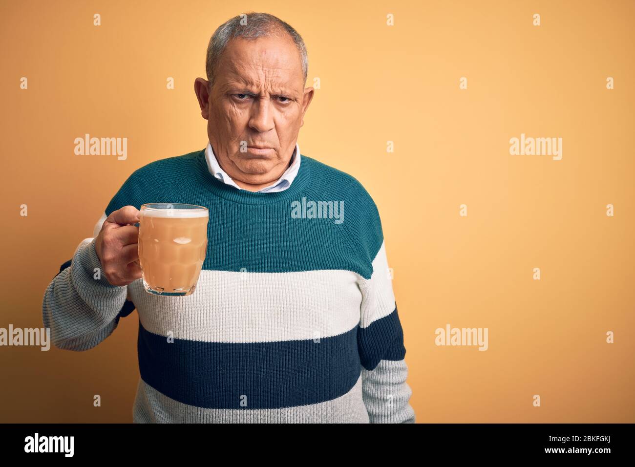Senior handsome man drinking jar of beer standing over isolated yellow ...