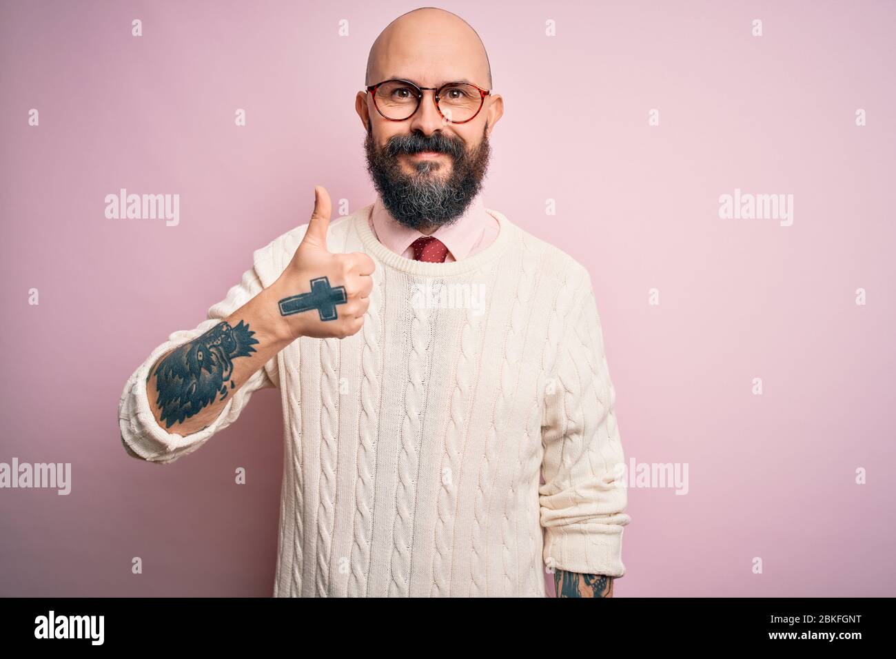 Handsome bald man with beard and tattoo wearing glasses and sweater ...