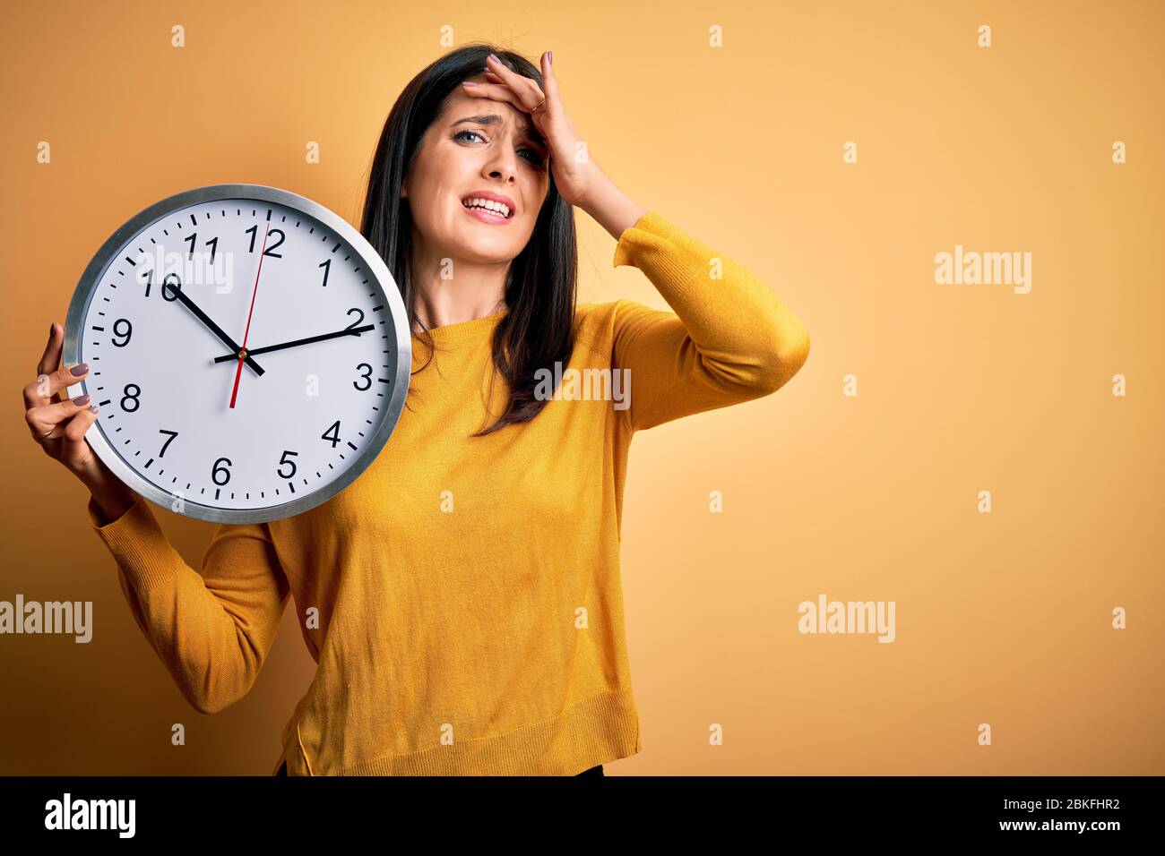 Young woman with blue eyes doing countdown holding big clock over ...