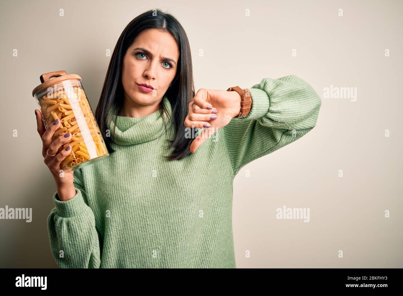 Young brunette woman holding dry italian macaroni over brown isolated ...