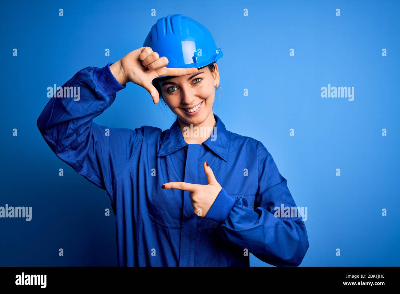 Young beautiful worker woman with blue eyes wearing security helmet and ...