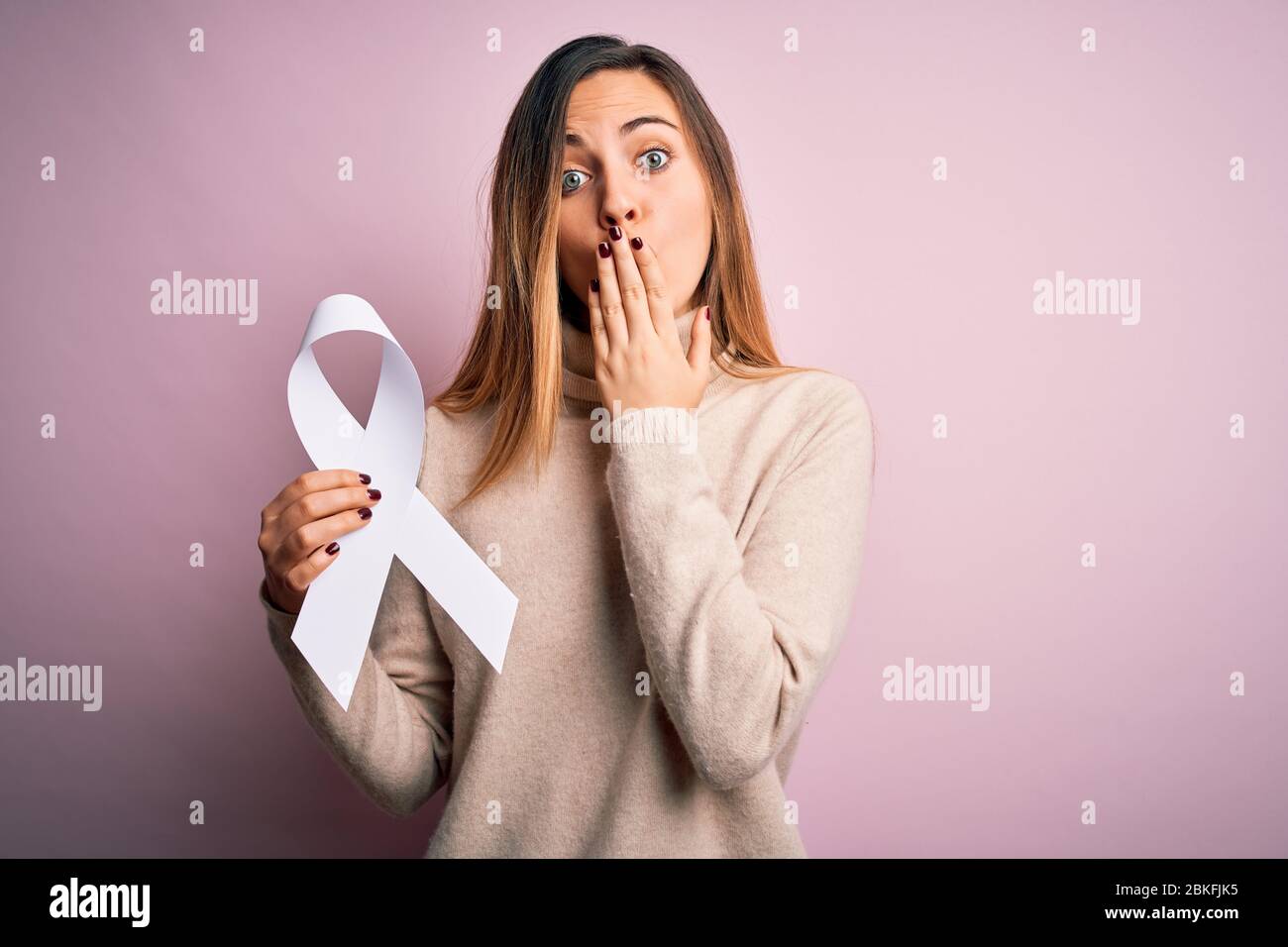 Young beautiful blonde woman with blue eyes holding white ribbon over ...