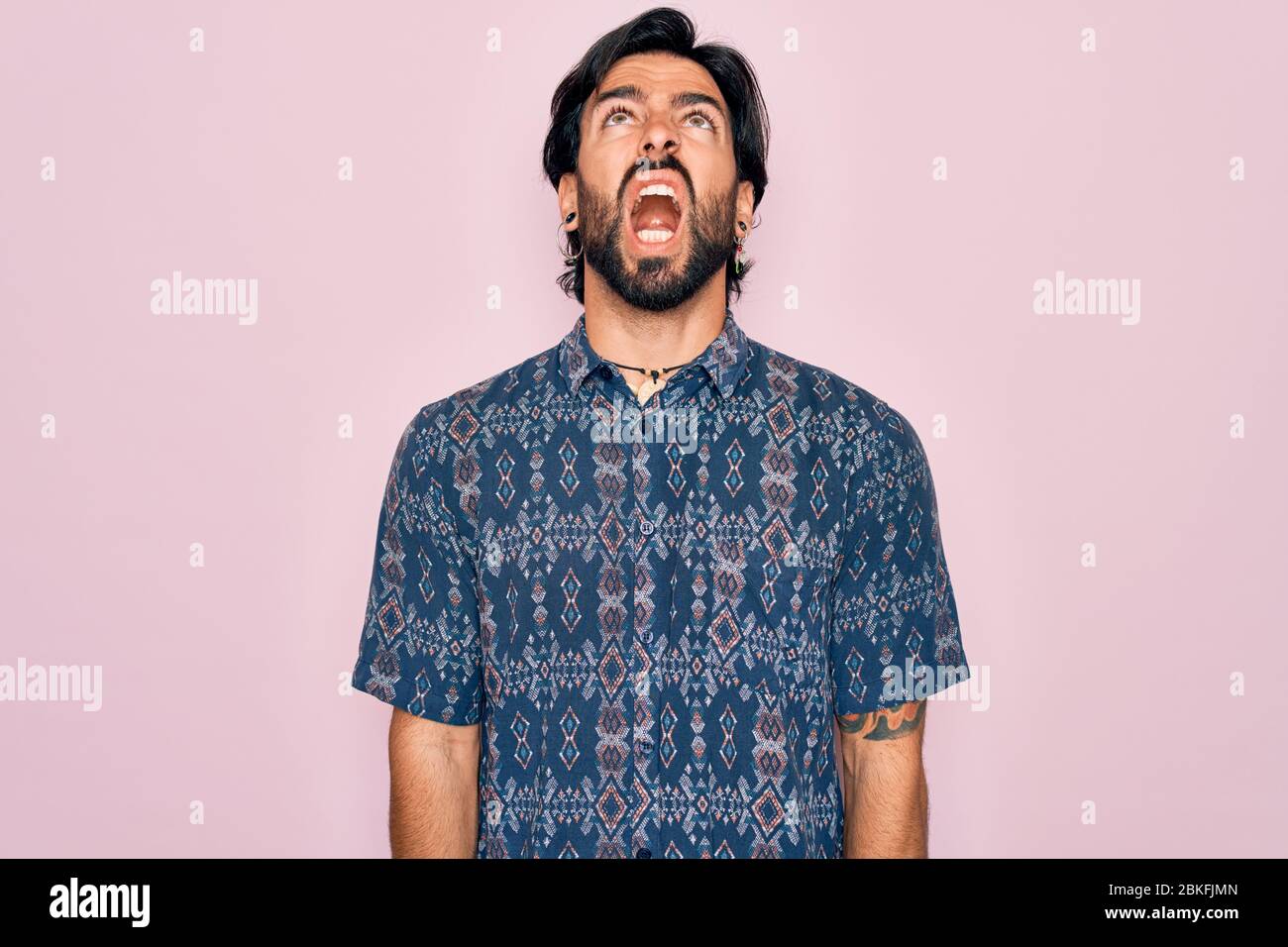 Young handsome hispanic bohemian man wearing hippie style over pink ...