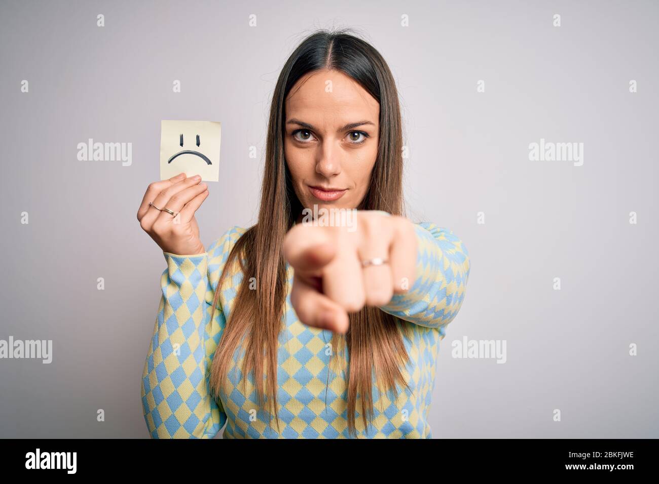 Young blonde woman holding sticky paper note with sad face emoticon ...