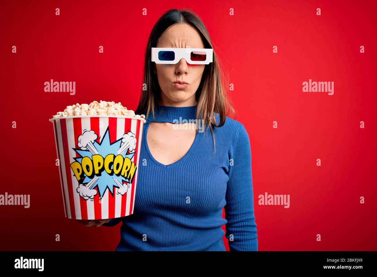 Young blonde woman wearing 3d glasses and eating pack of popcorn ...
