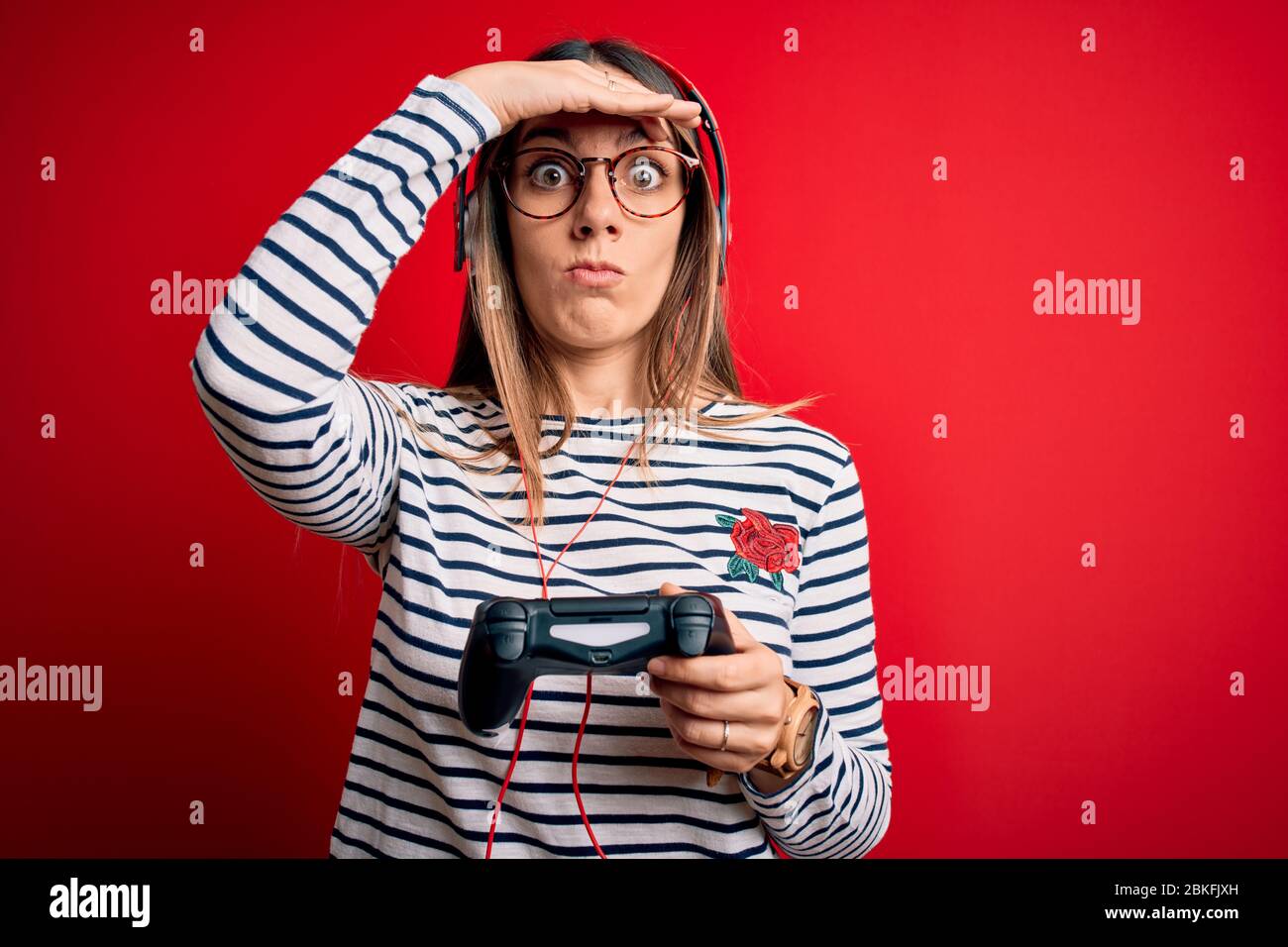 Young blonde gamer woman using gamepad playing video games over red ...