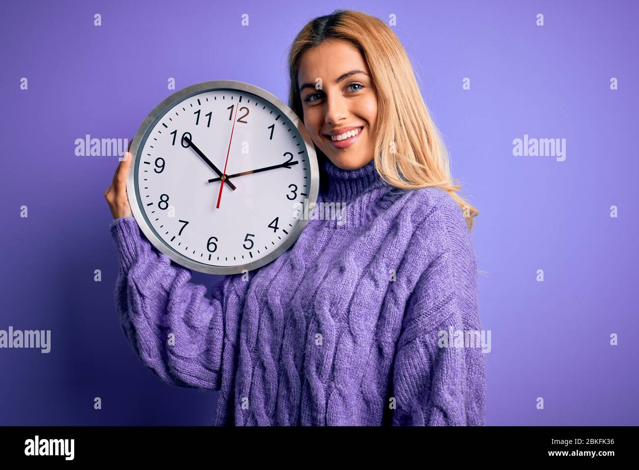 Young beautiful blonde woman doing countdown holding big clock over ...