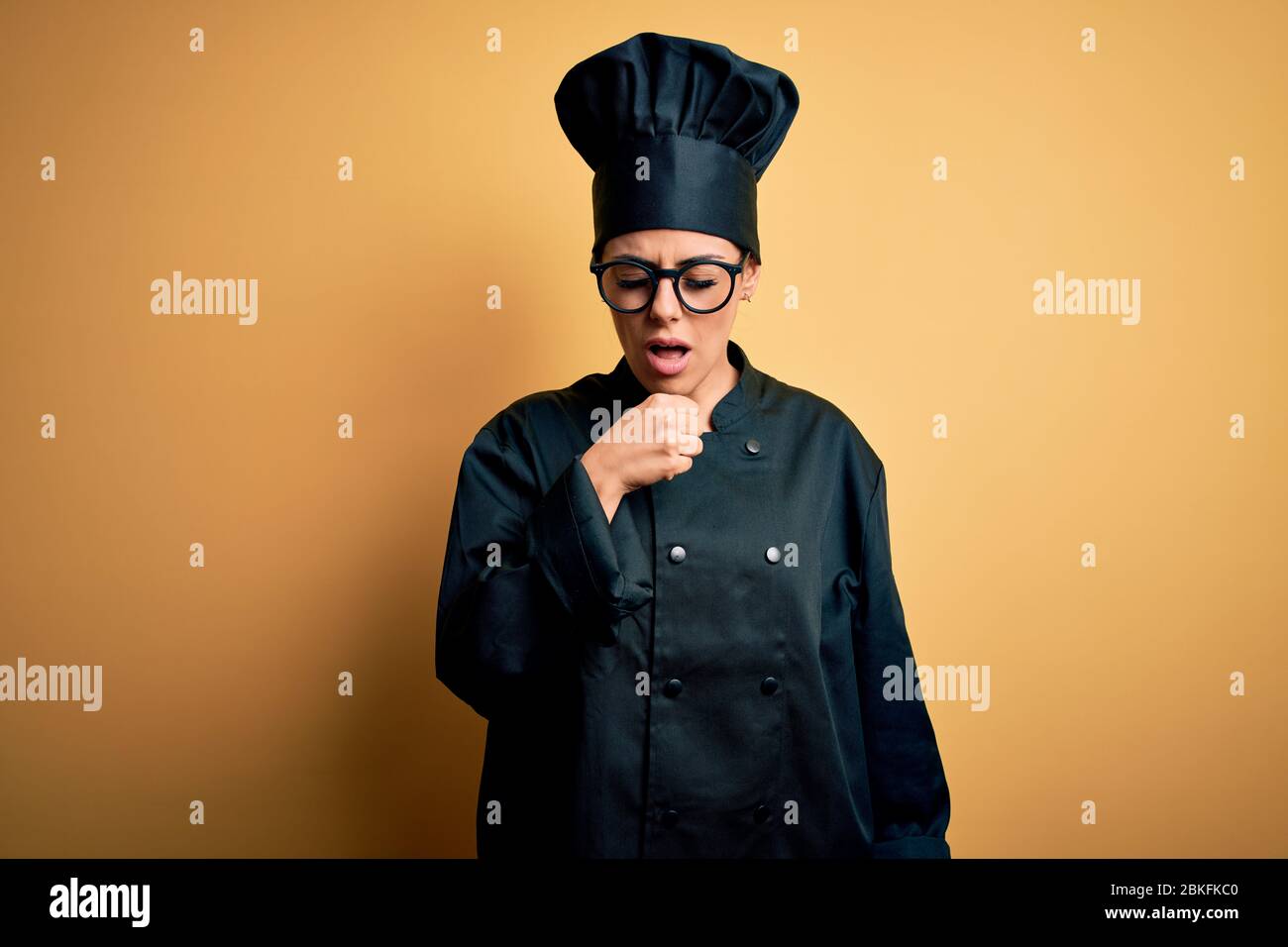 Young beautiful brunette chef woman wearing cooker uniform and hat over ...