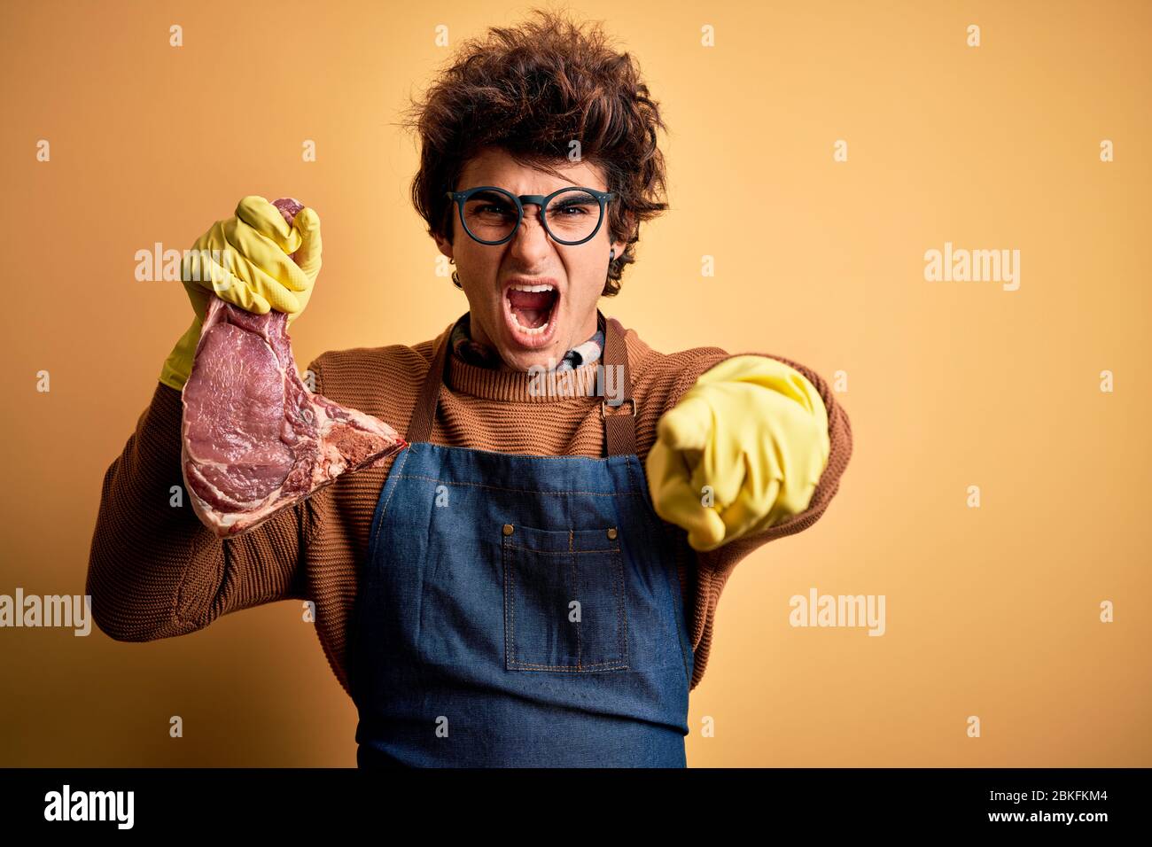 Young handsome butcher man holding meet steak standing over isolated ...