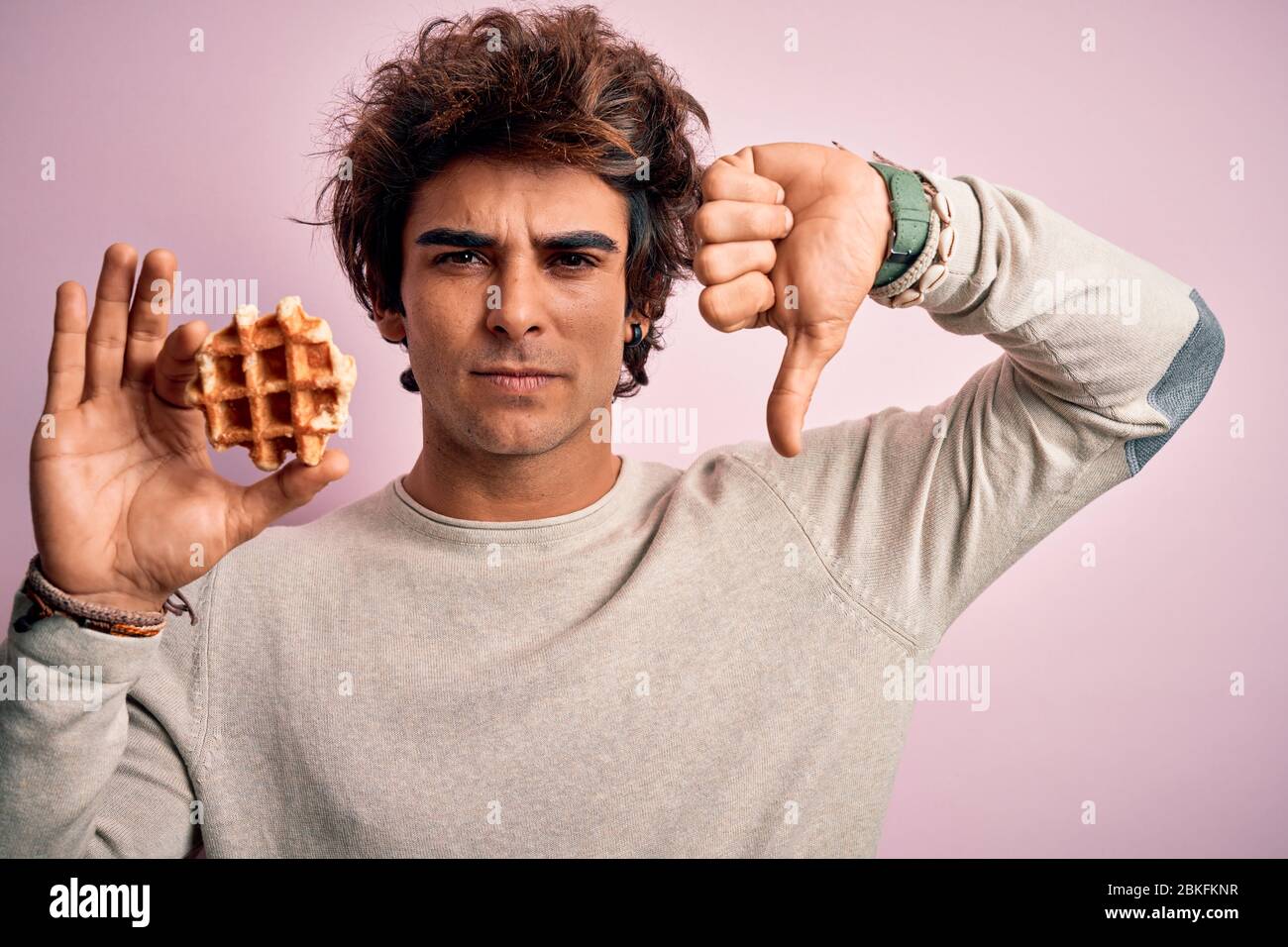 Young handsome man holding sweet waffle standing over isolated pink ...