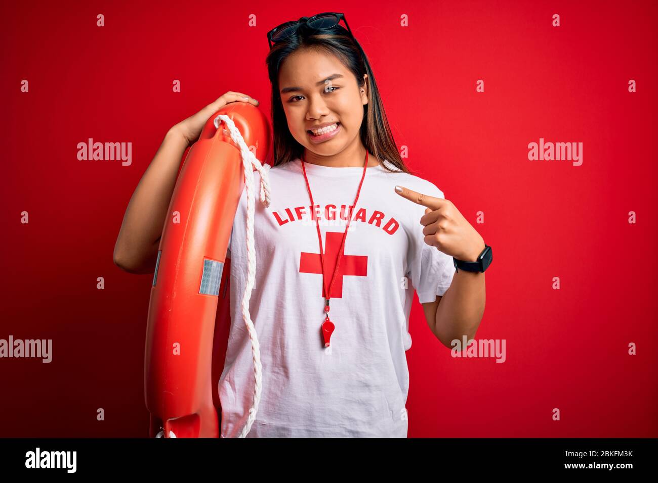 Young asian lifeguard girl wearing t-shirt with red cross using whistle ...