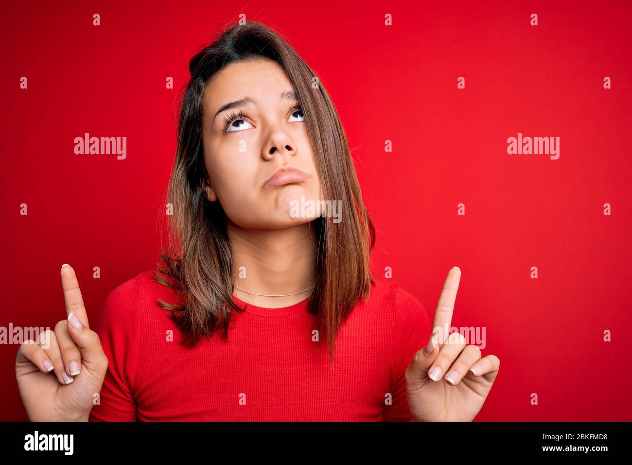 Young beautiful brunette girl wearing casual t-shirt over isolated red ...
