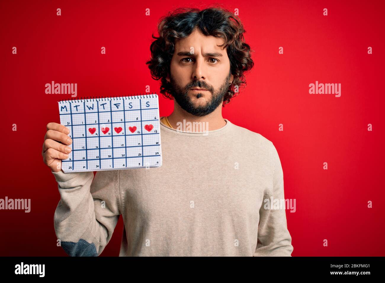 Young handsome man with beard holding calendar over isolated red ...