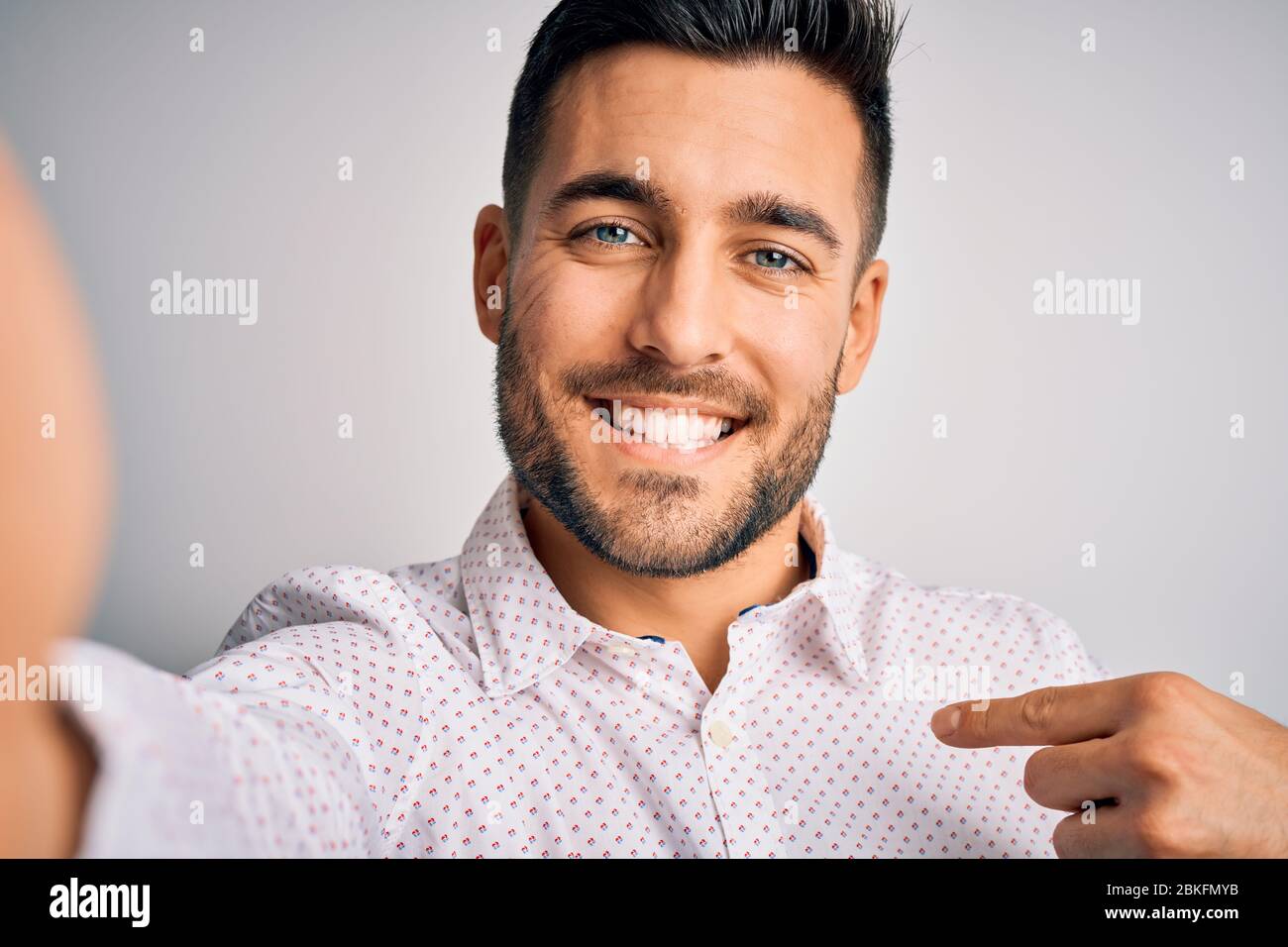 Young handsome man wearing shirt making selfie by the camera over white ...