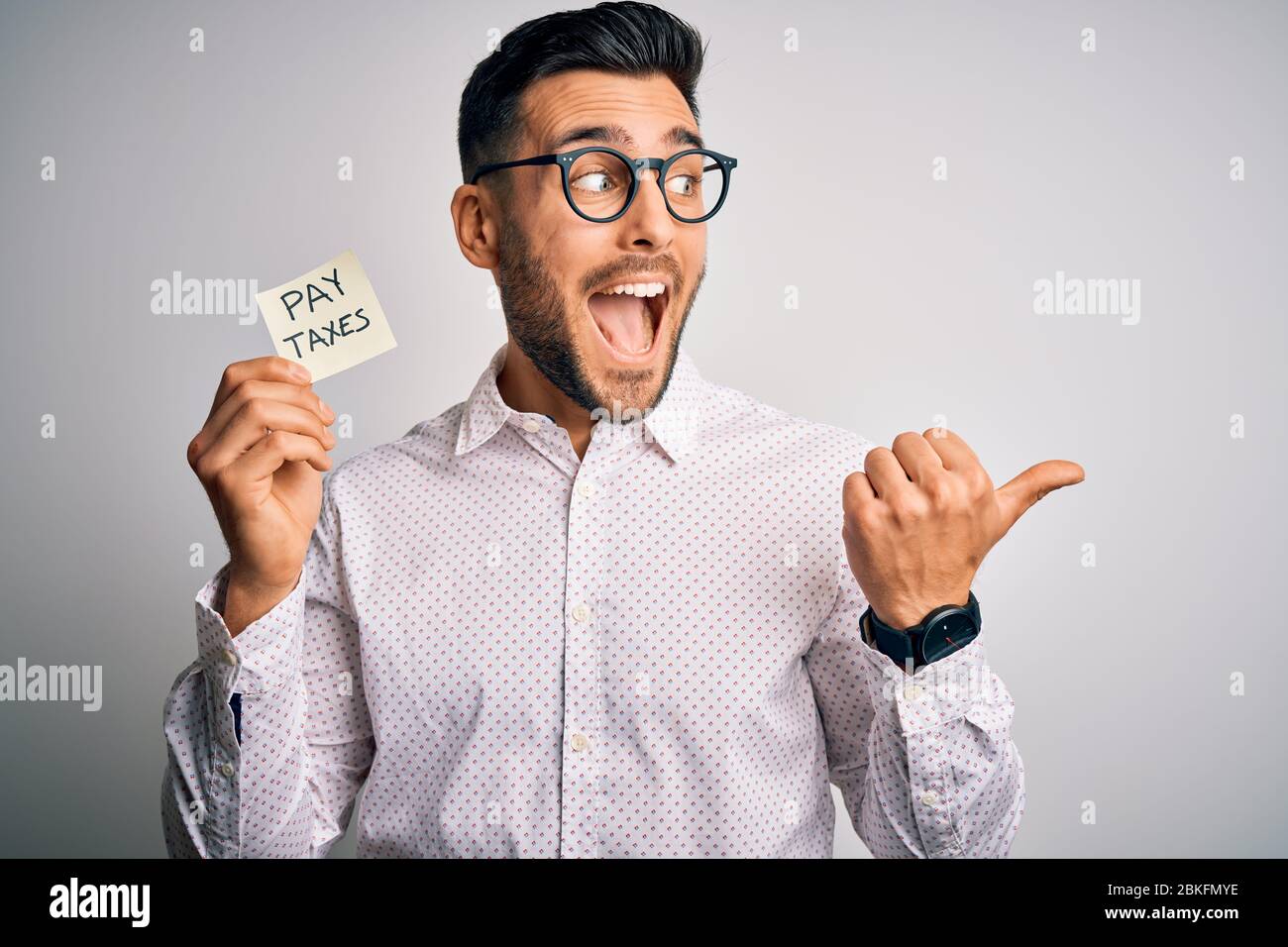 Young handsome man holding reminder paper with pay taxes message over ...