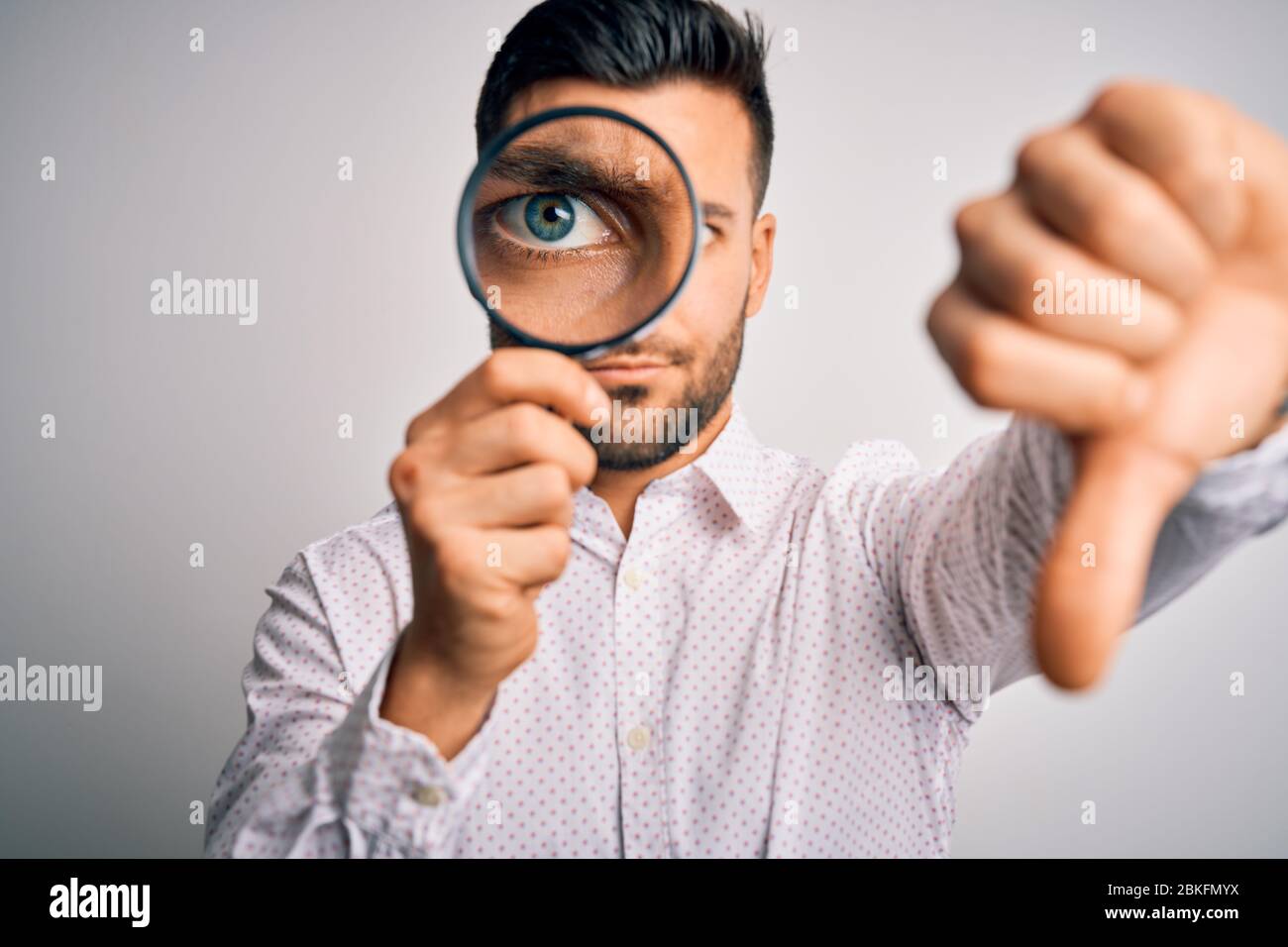 Young detective man looking through magnifying glass over isolated ...