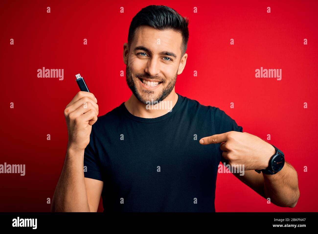 Young man holding USB memory data drive over red isolated background ...