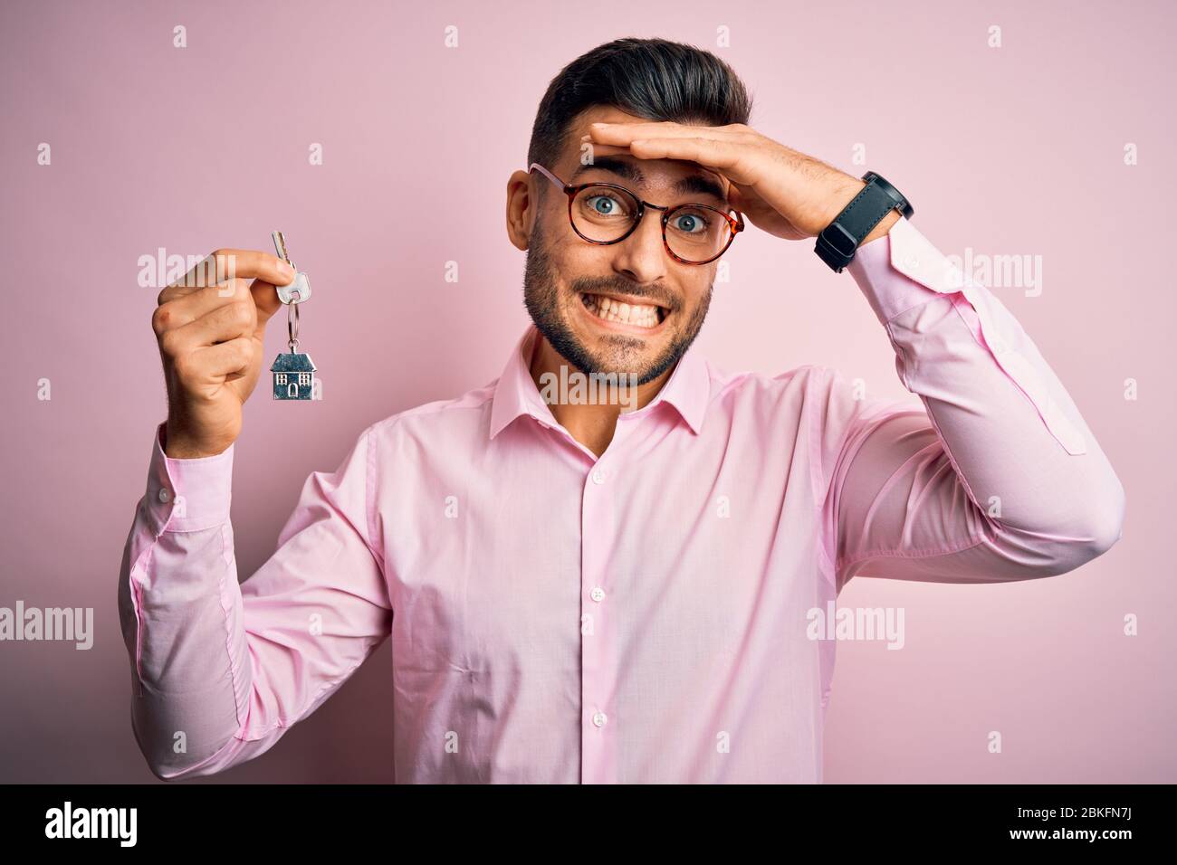 Young real estate business man holding new house keys over pink ...