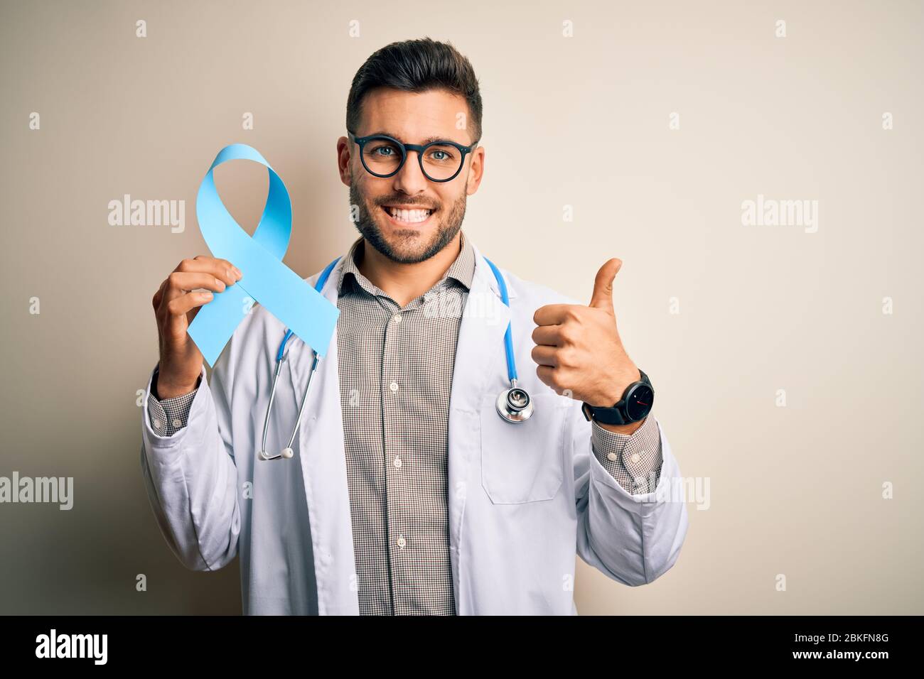 Young professional doctor man holding colon awareness blue ribbon over ...