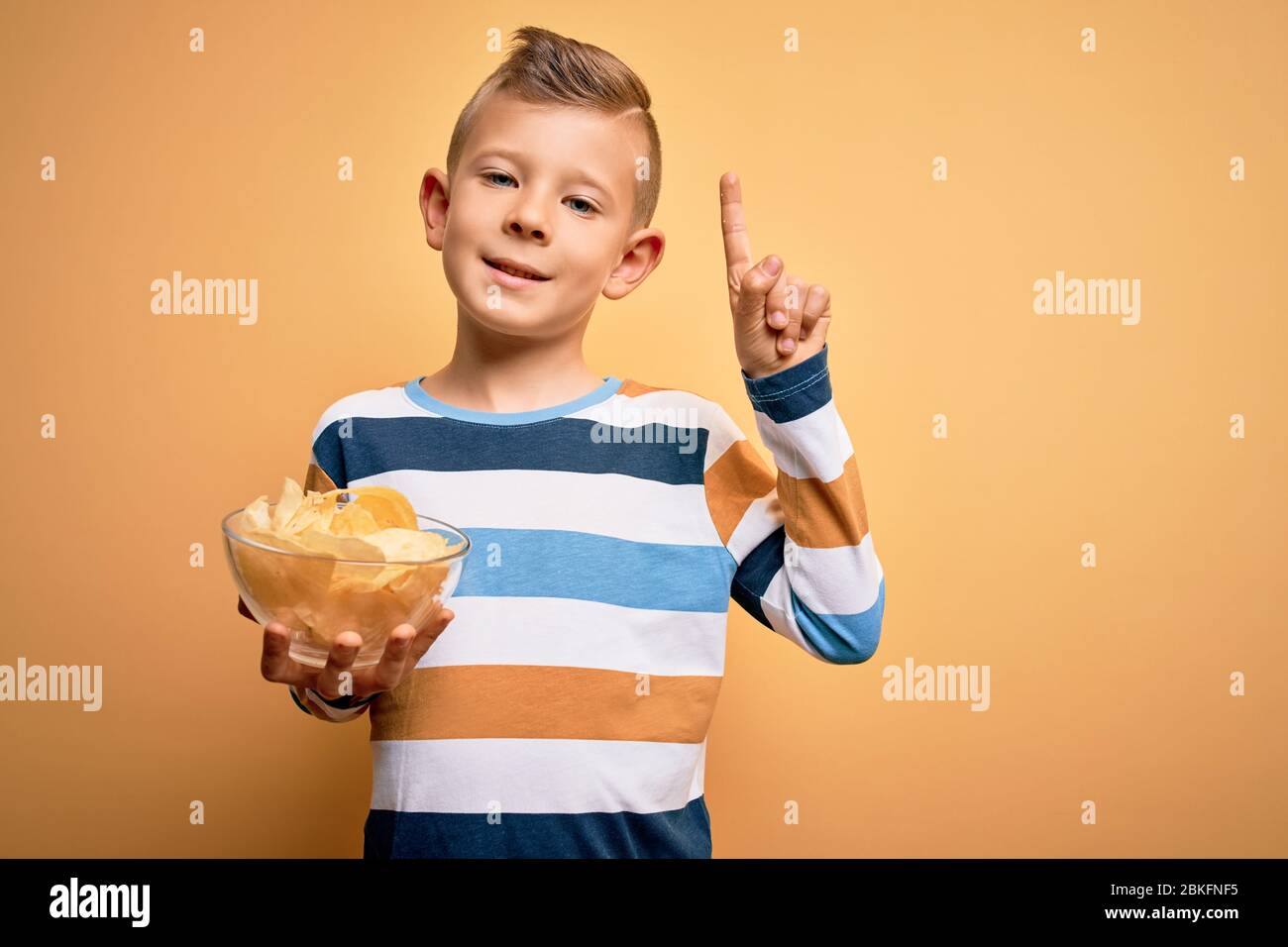 Young little caucasian kid eating unheatlhy potatoes crisps chips over ...