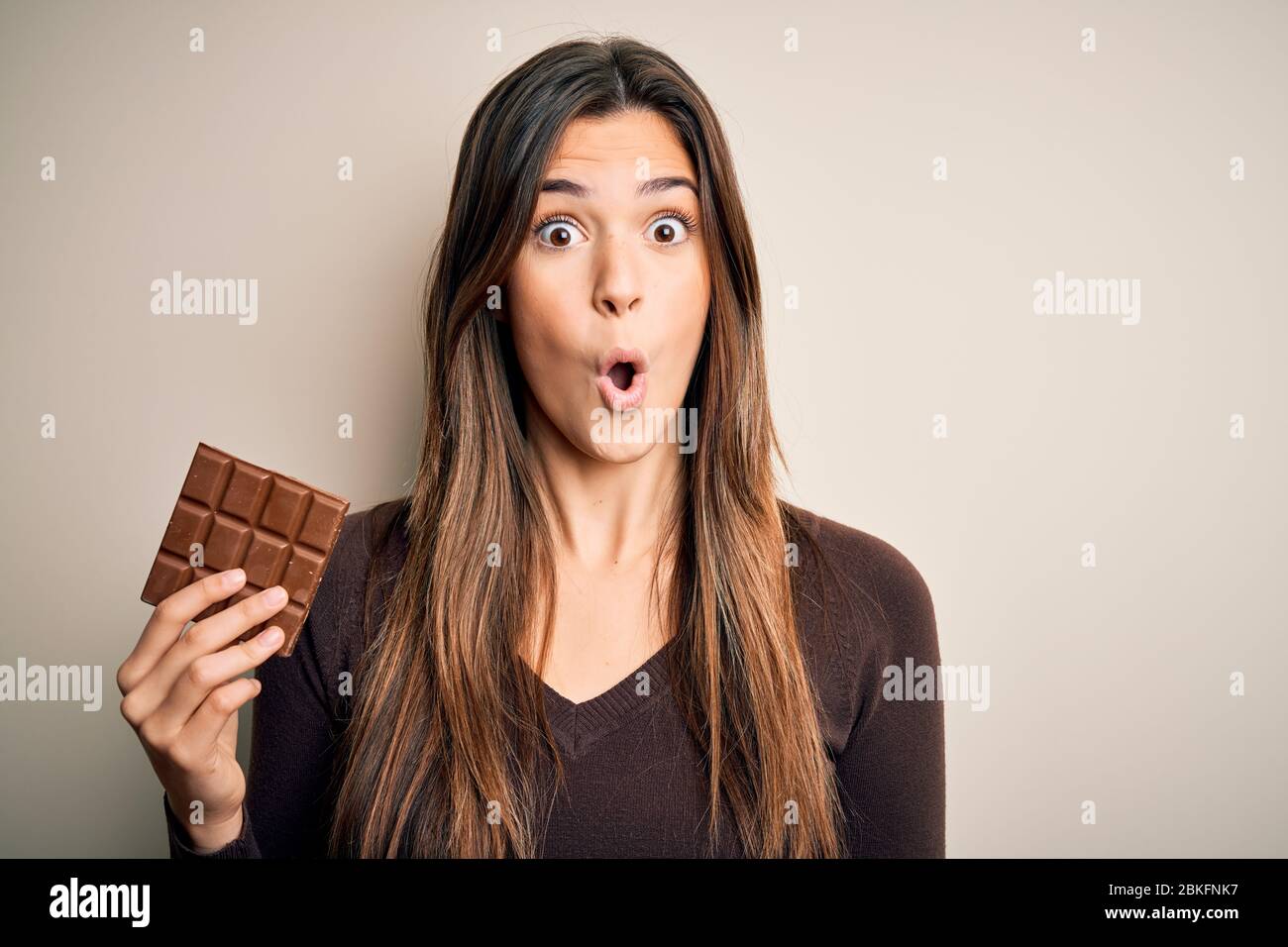 Young beautiful girl holding sweet bar of chocolate over isolated white ...
