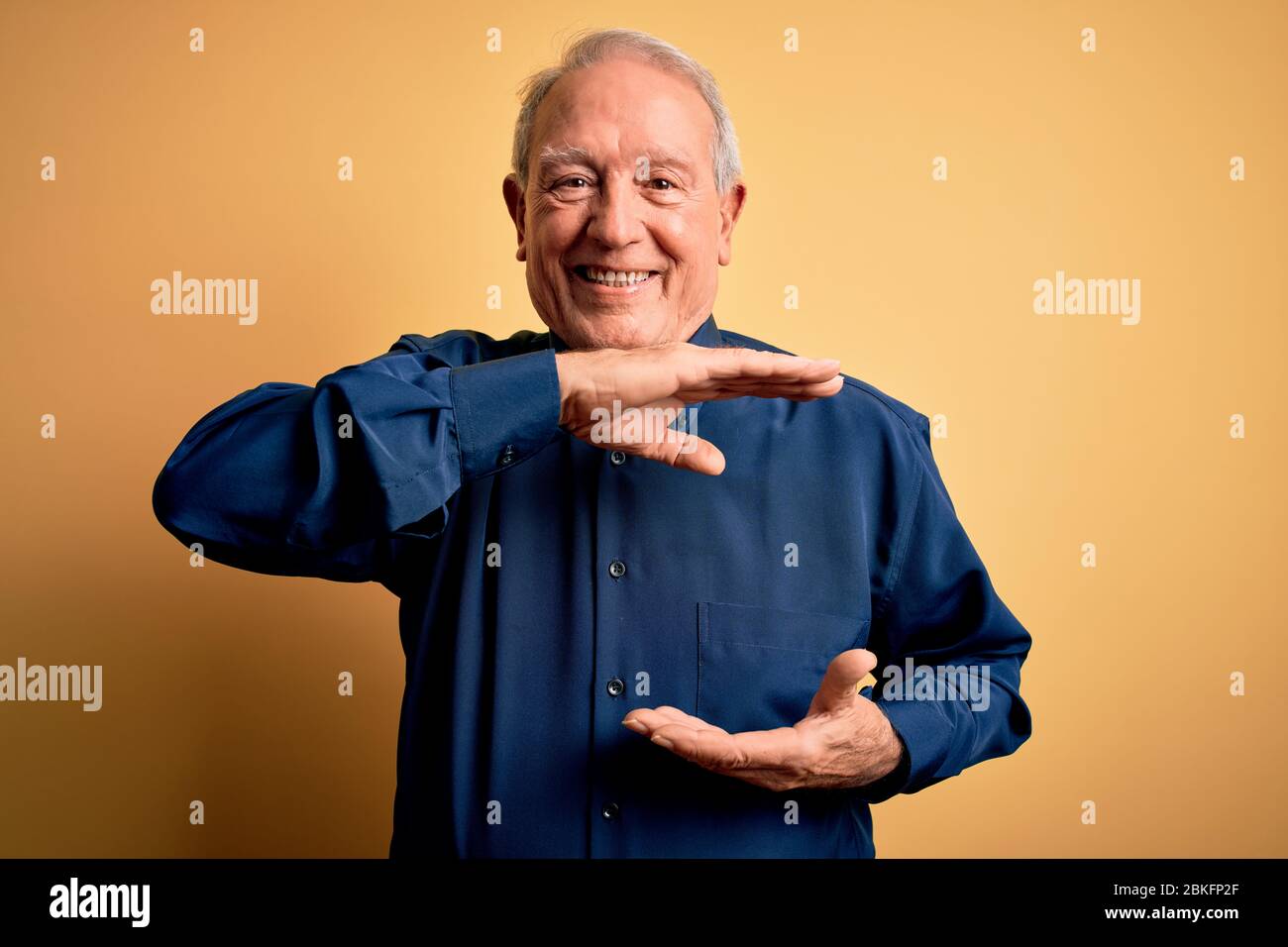 Grey haired senior man wearing casual blue shirt standing over yellow ...