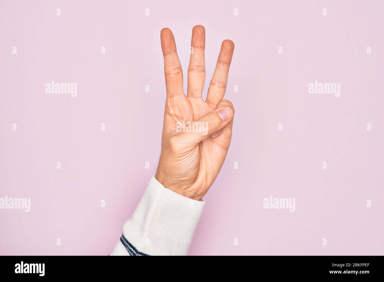 Hand of caucasian young man showing fingers over isolated pink background counting number 3 ...