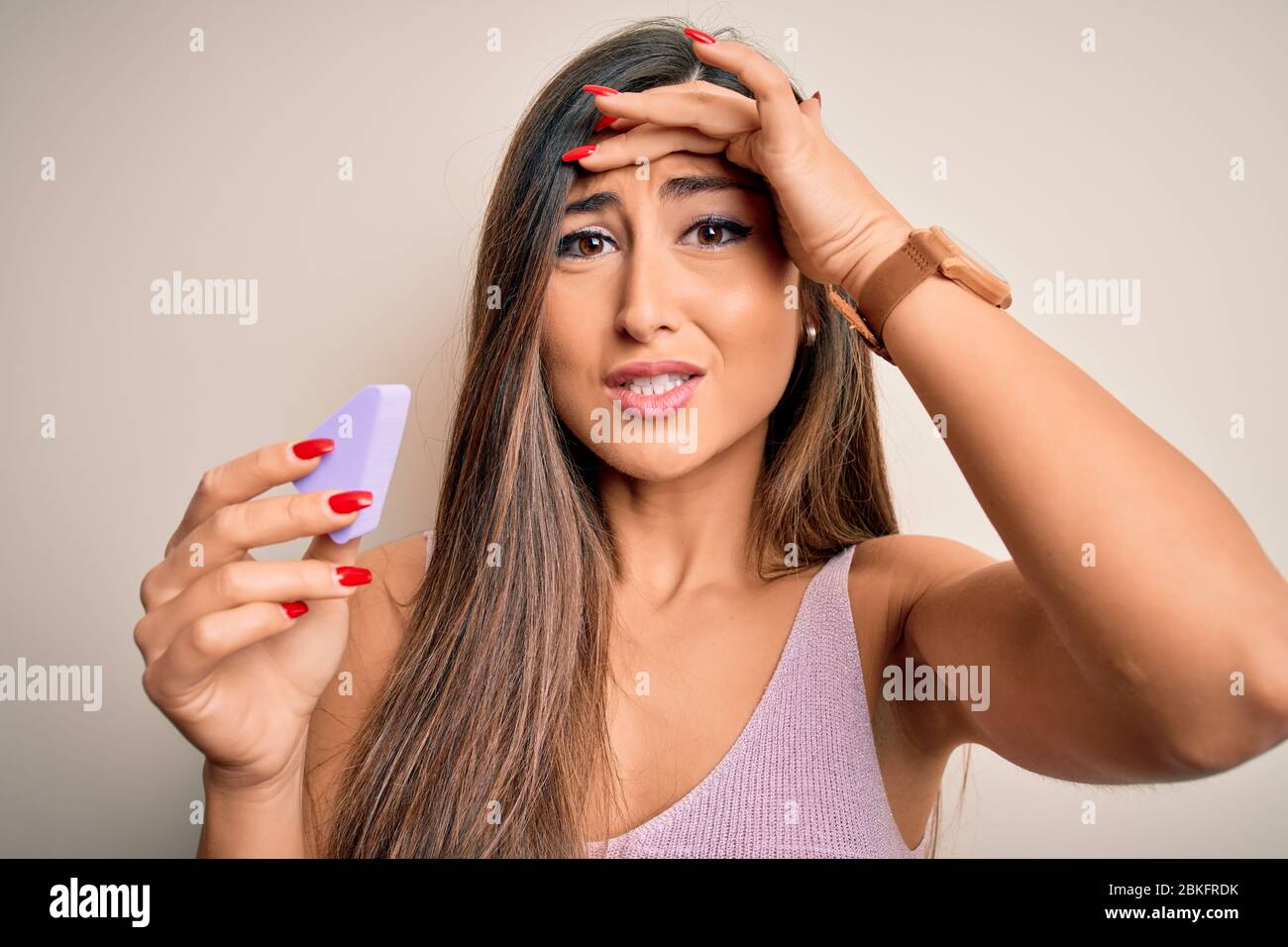 Young beautiful woman using beauty sponge with facial makeup over pink ...
