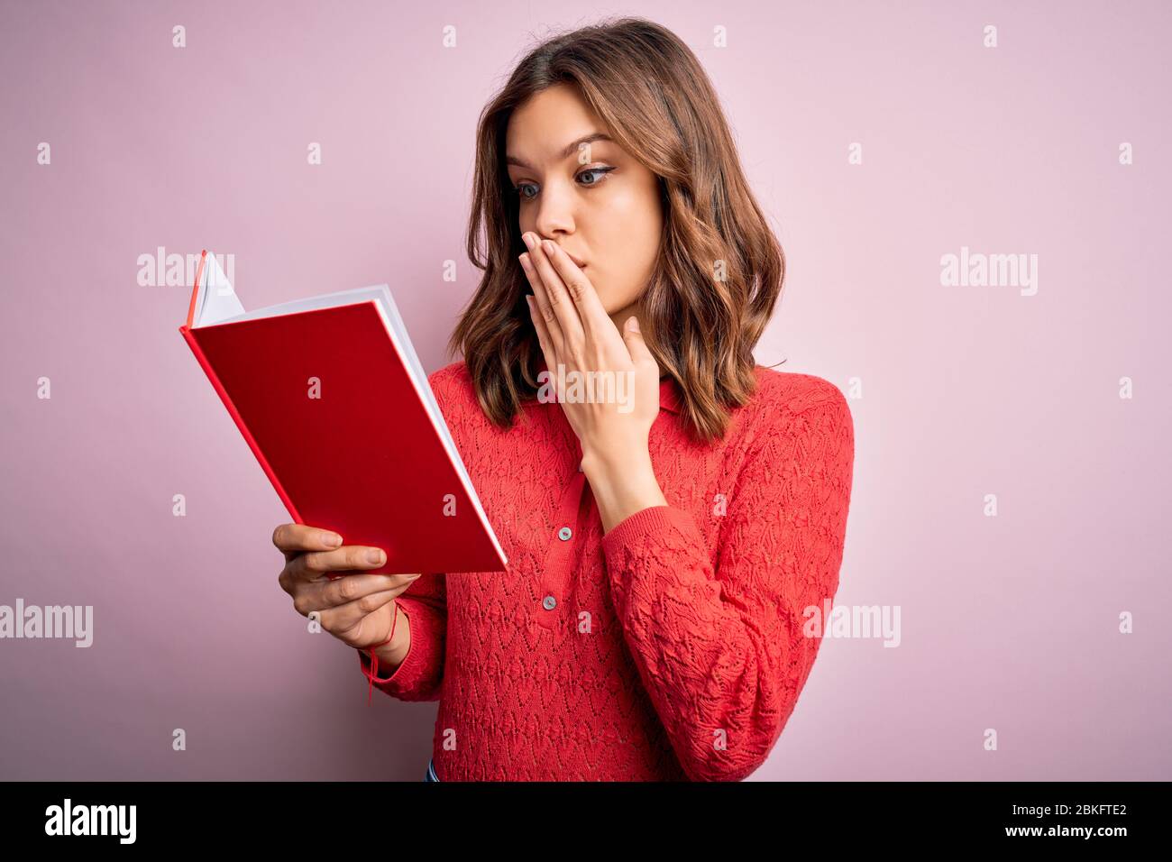 Young blonde student girl reading a book over pink isolated background ...