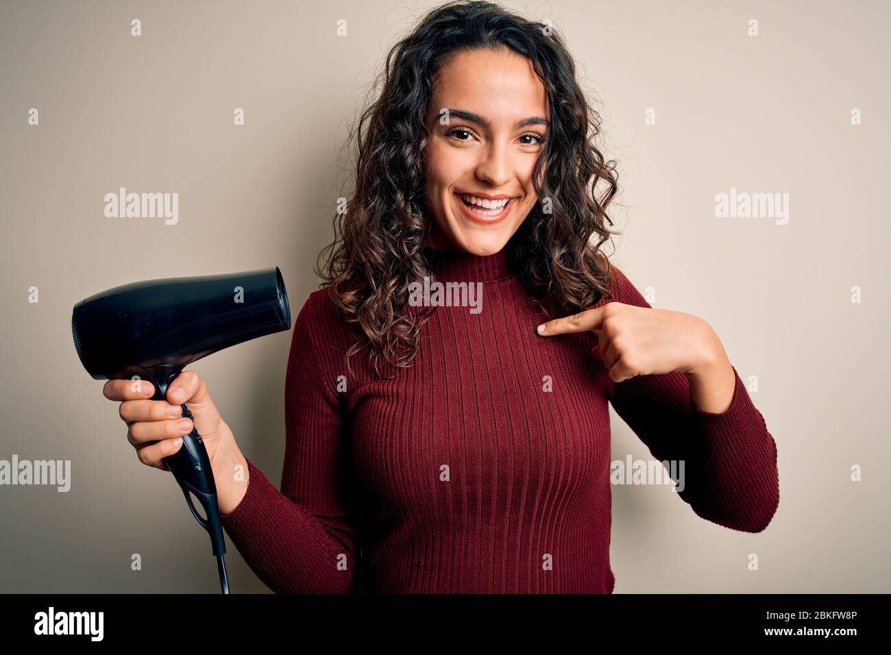 Young beautiful woman with curly hair using hair dryer over isolated ...