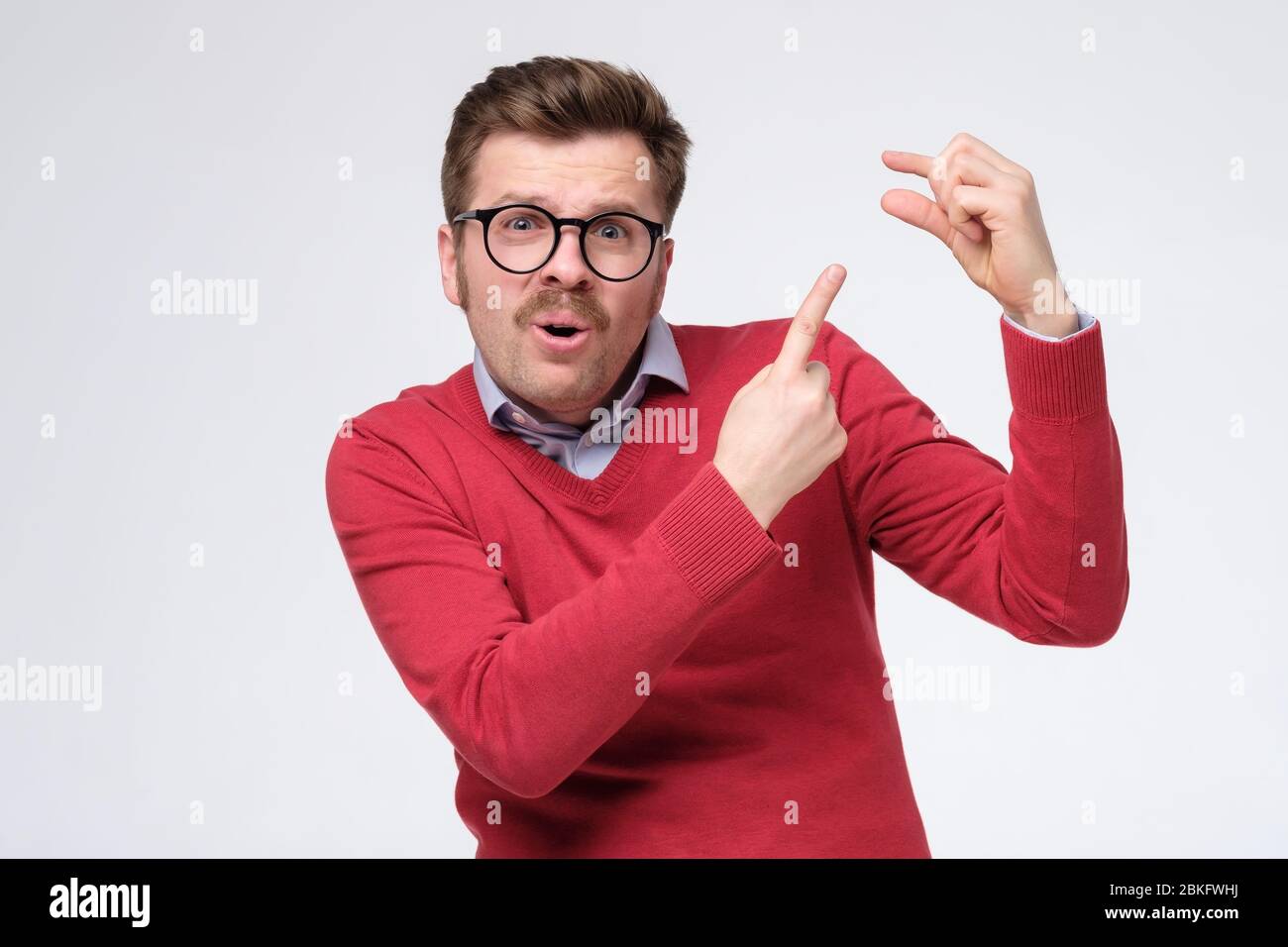 Young caucasian man gesturing with hand showing small size sign with ...