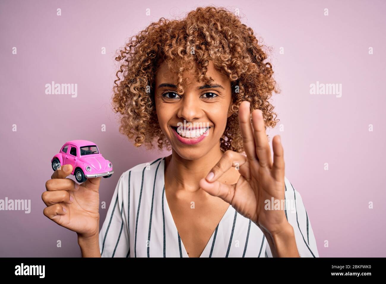 Young african american woman holding small pink car standing over ...