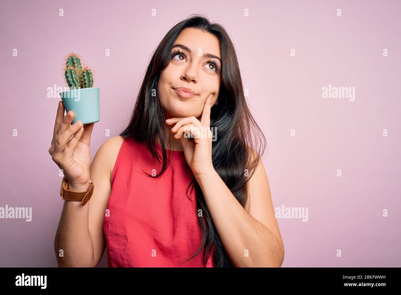 Young brunette woman holding succulent cactus plant over pink ...
