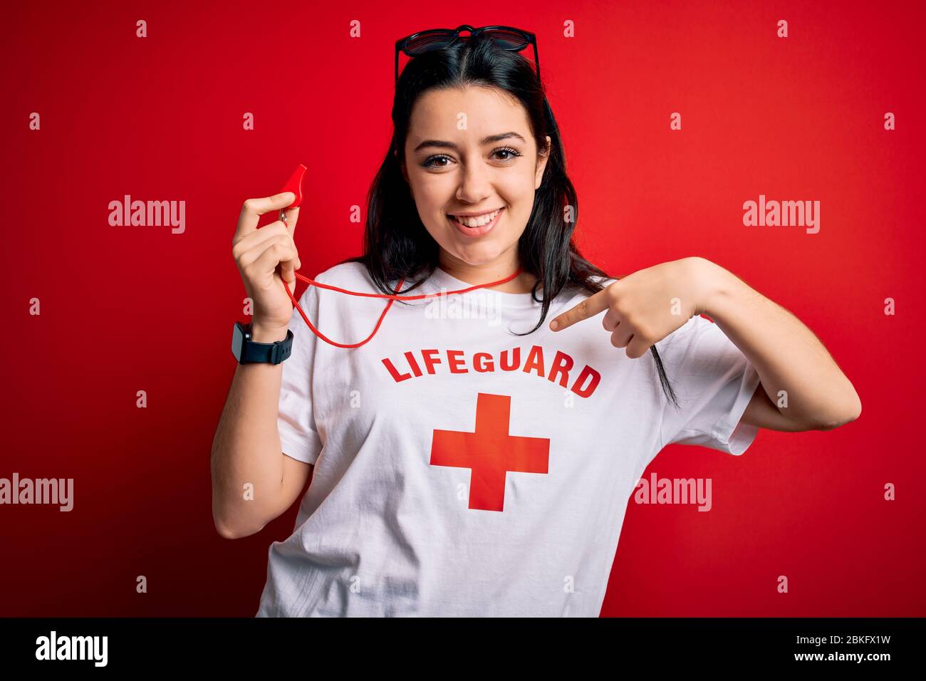 Young lifeguard woman wearing guard equipement holding whistle over red ...