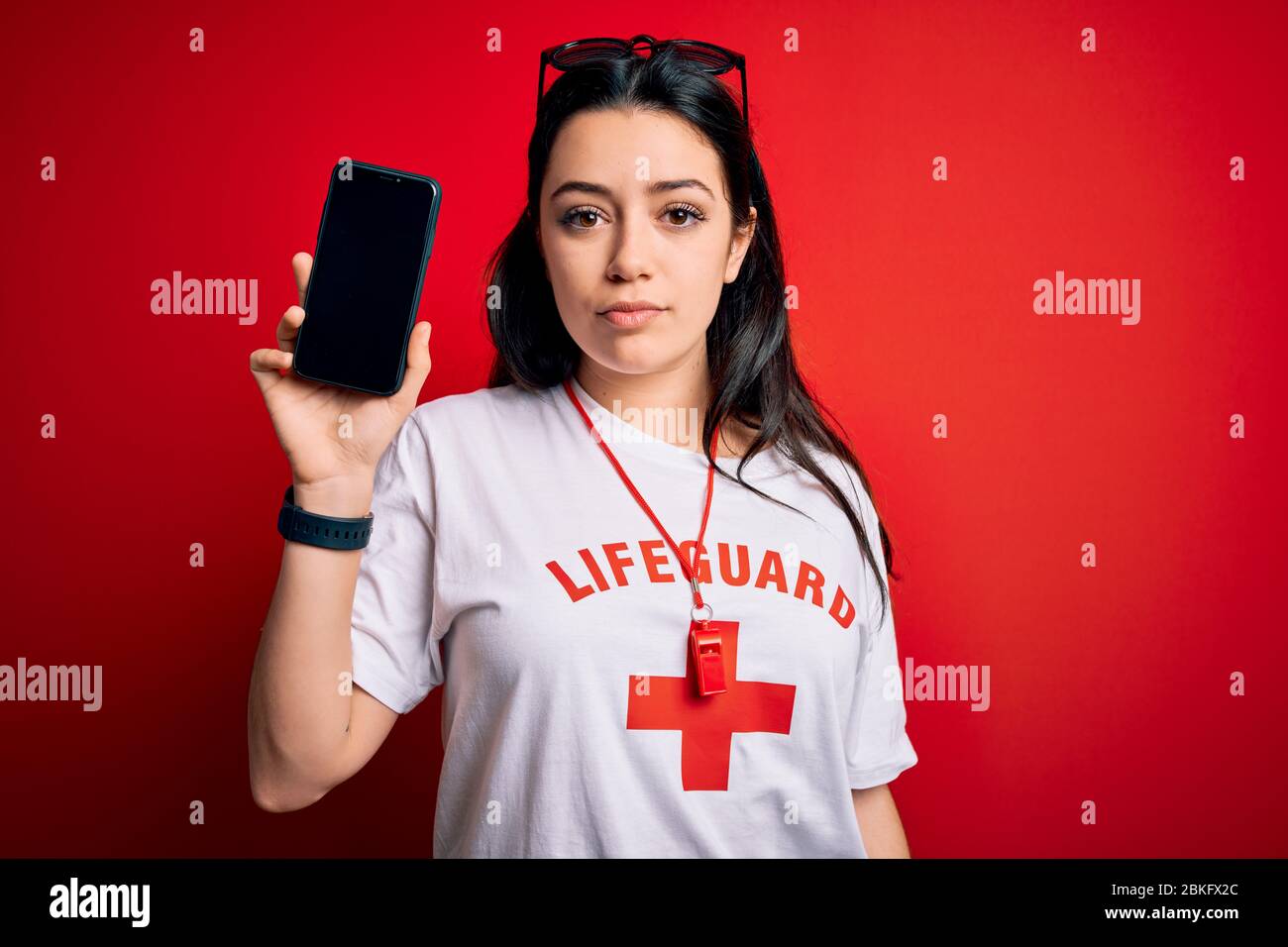 Young lifeguard woman showing smartphone screen over red background ...