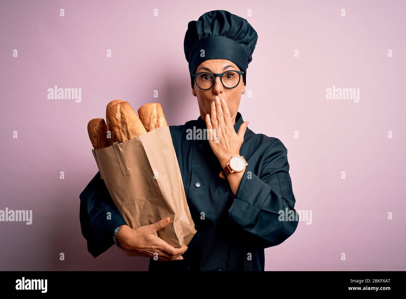 Middle age baker woman wearing cooker uniform and hat holding paper bag ...