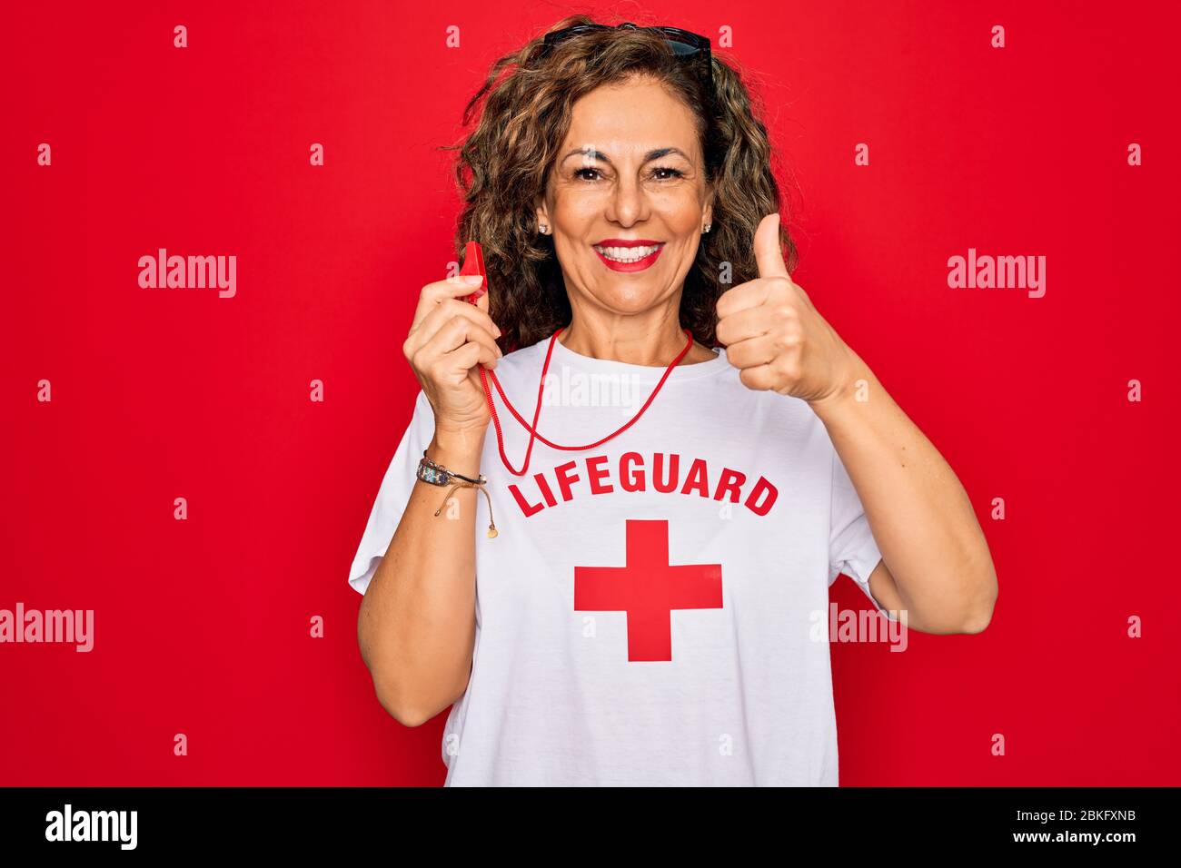 Middle age senior summer lifeguard woman holding whistle over red ...